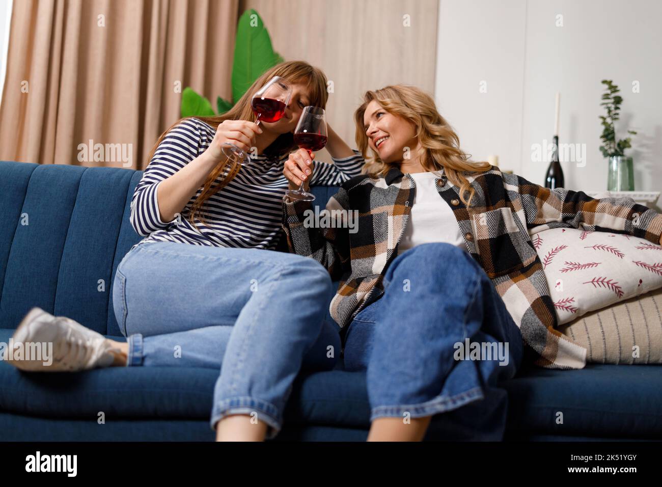 Two women of different ages have fun and friendly gossip and drink wine ...