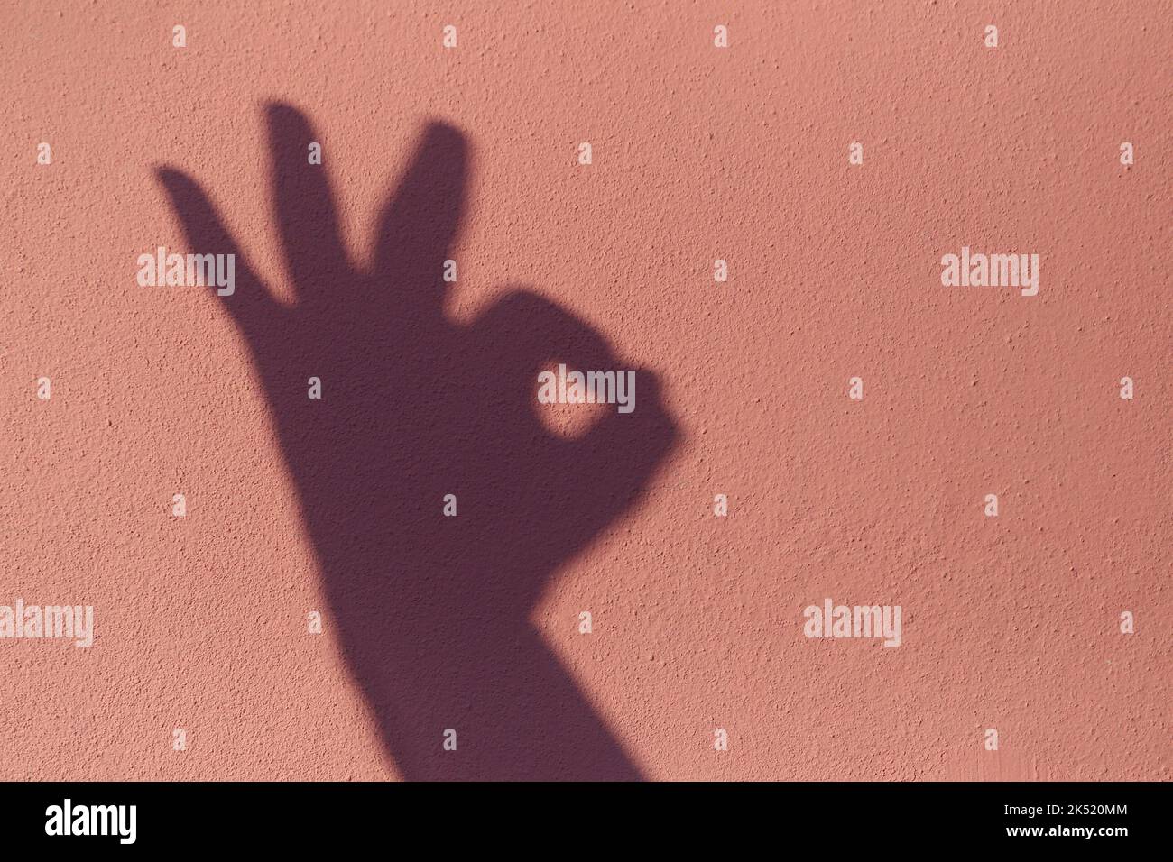 Shadow of the hand that made the ok sign on pink concrete background ...