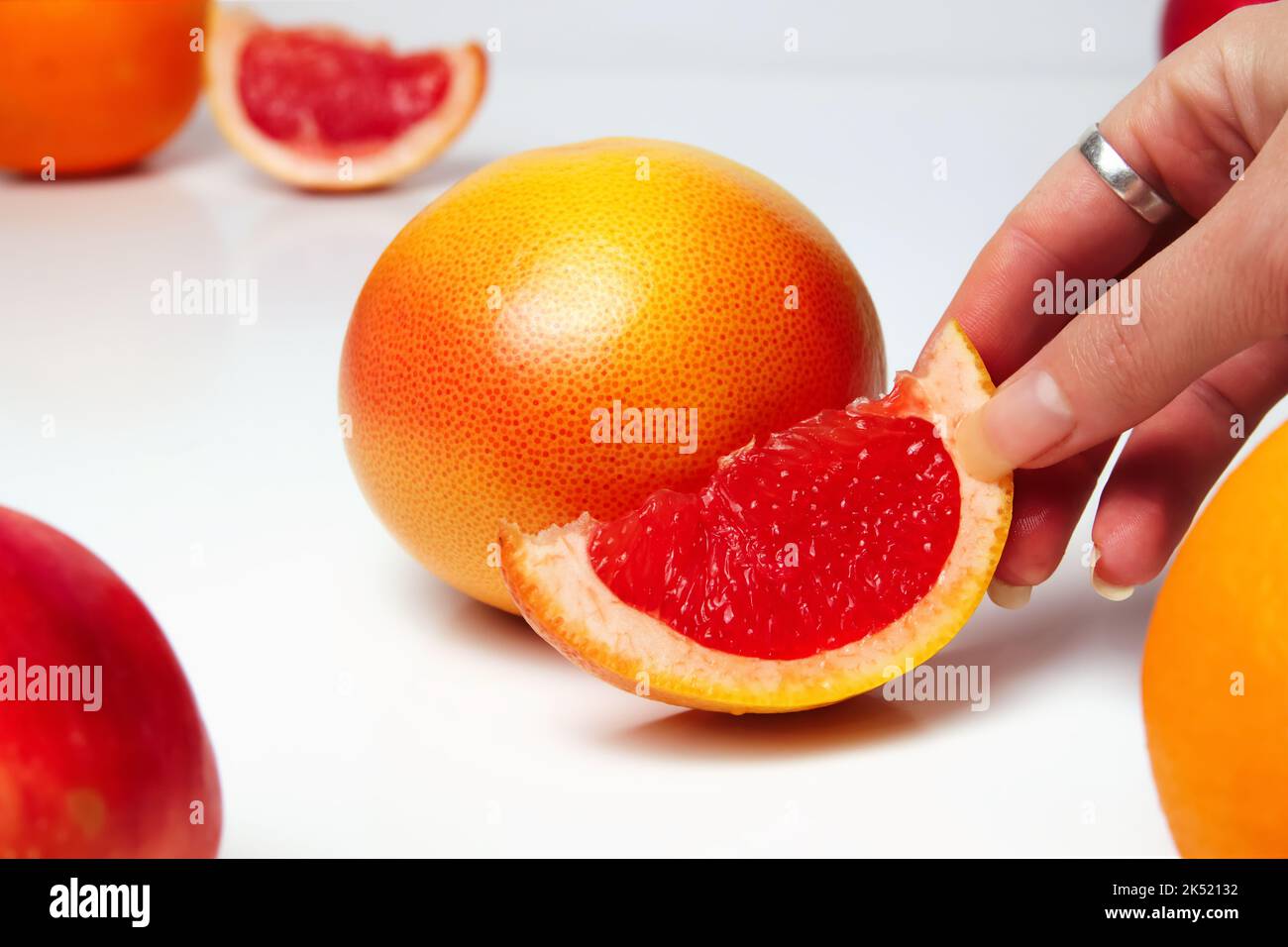 Defocus female hand holding piece of a red grapefruit on white ...