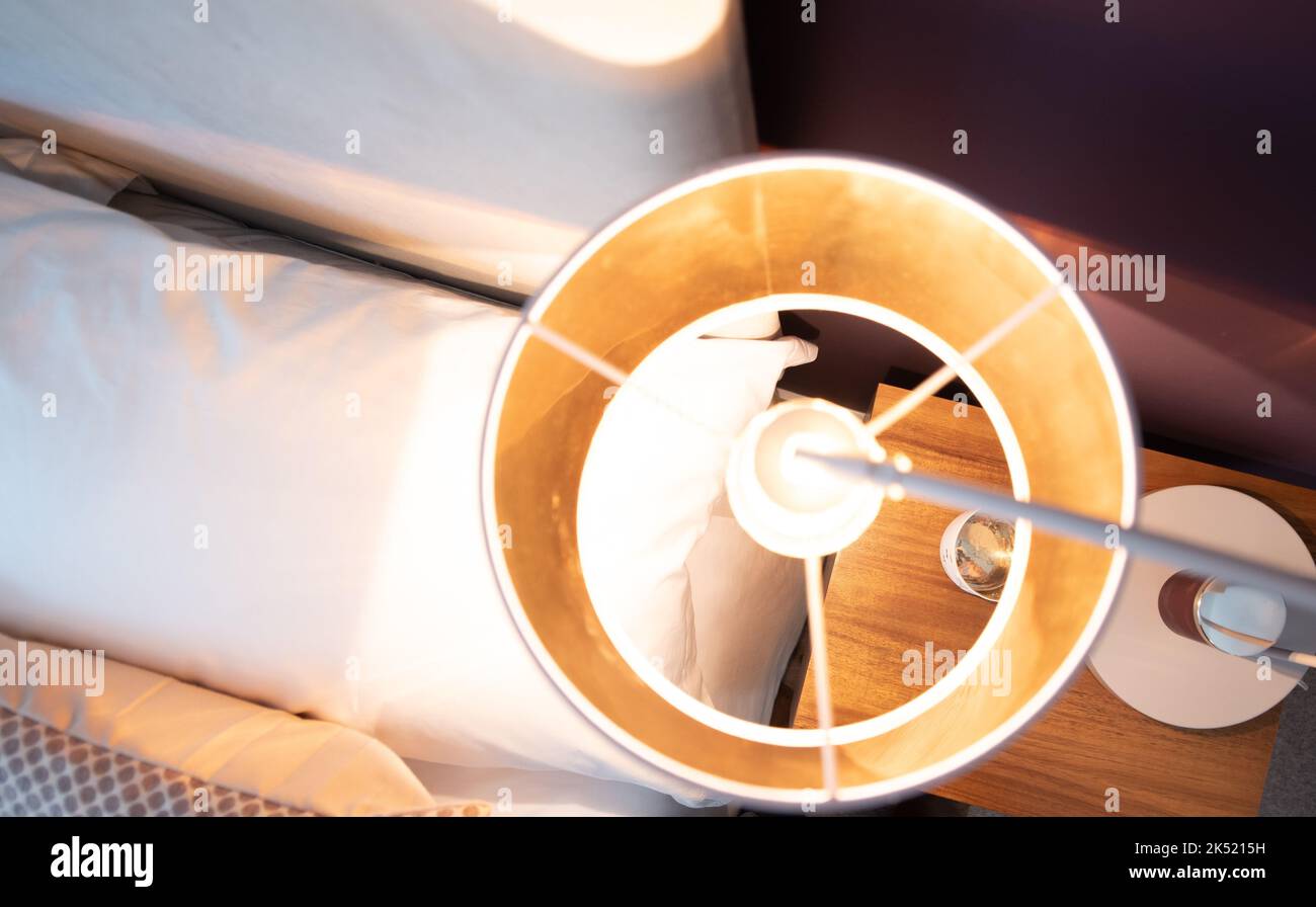 A high angle shot of a bright lamp on a wooden table beside a bed ...