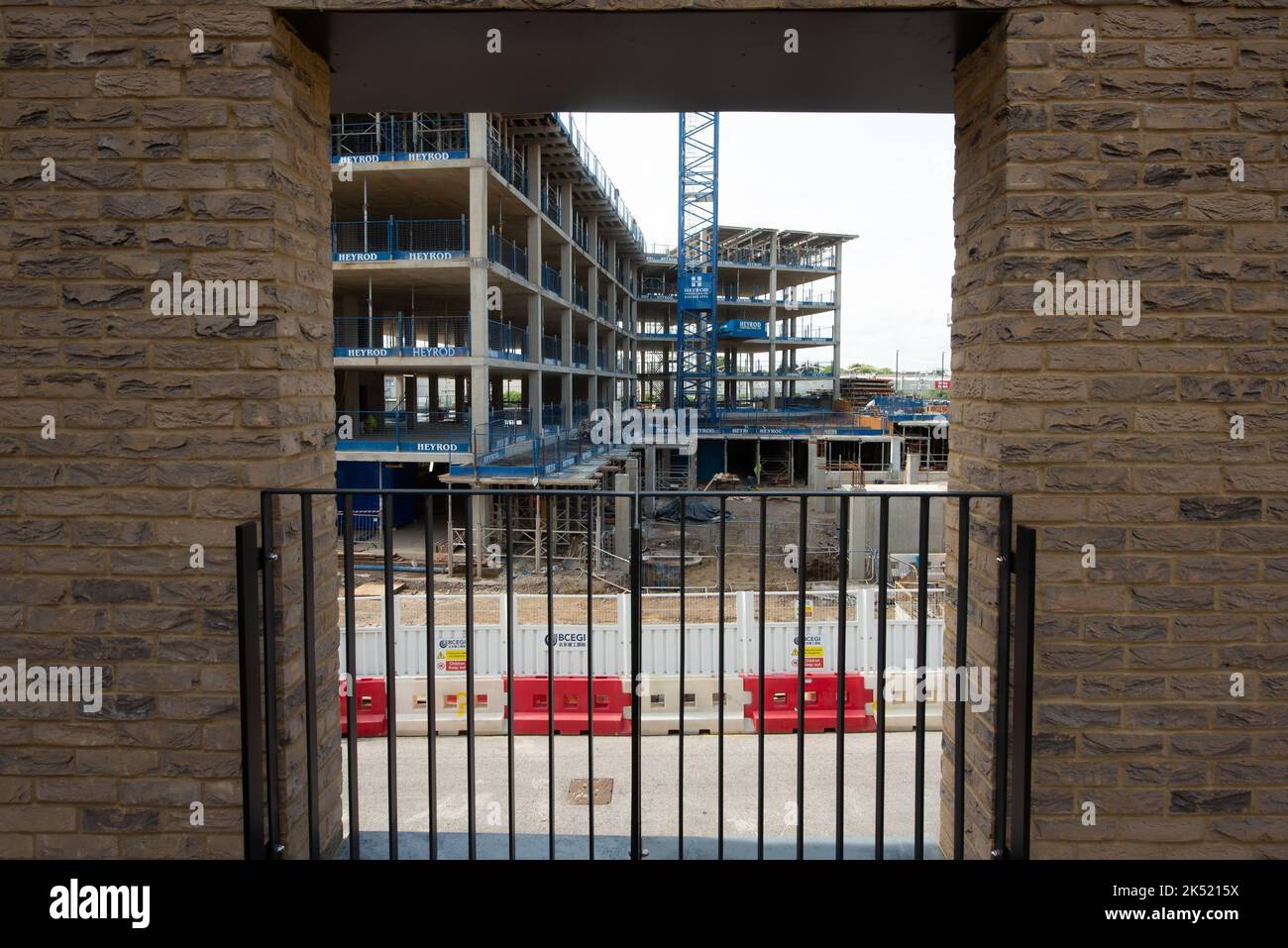 A metal fence between brick walls with cranes during construction on a ...