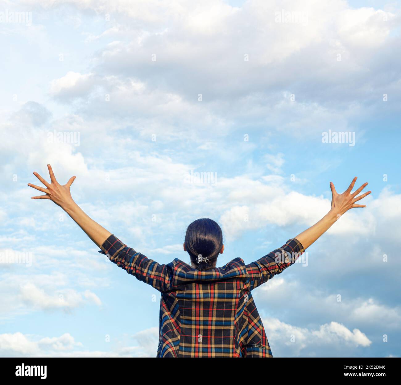 A young woman stretches her arms up against the sky while standing with ...