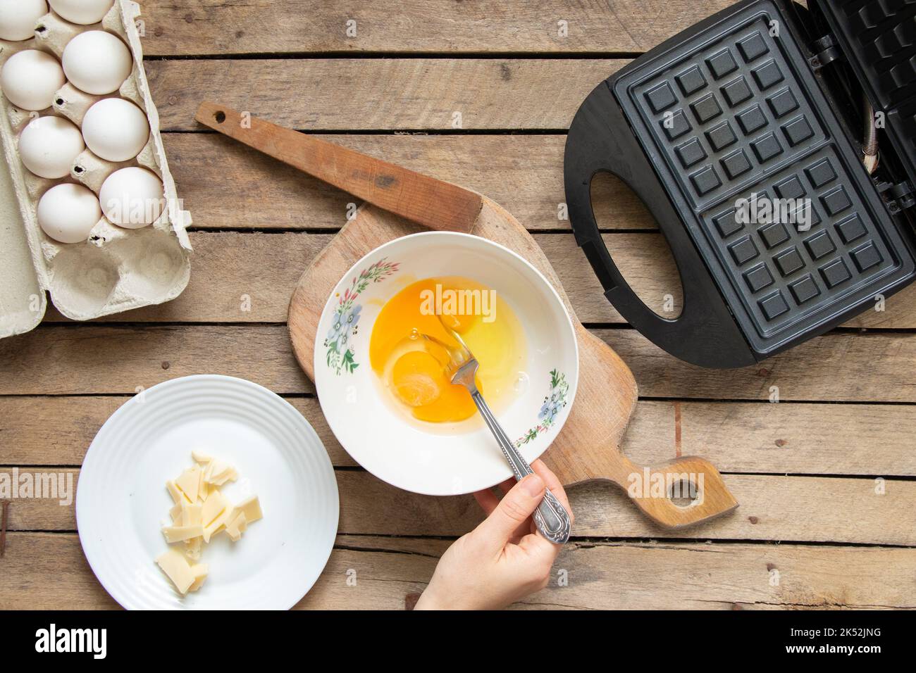 fry scrambled eggs with cheese and spices in a waffle iron on a wooden ...