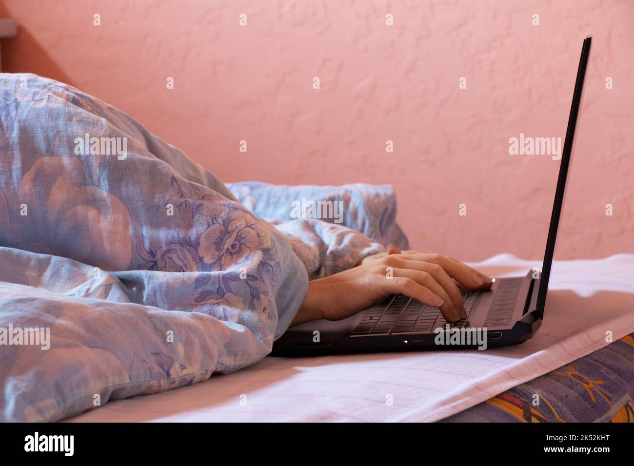 female hands on the laptop keyboard on the bed in a blanket, working at ...