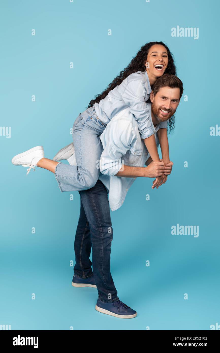 Laughing young european male holding on back middle eastern woman, have ...