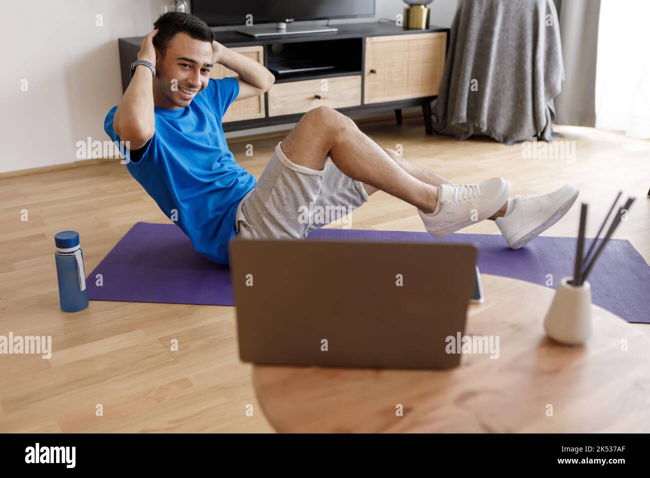 Active young middle eastern man in sportswear exercising at home ...