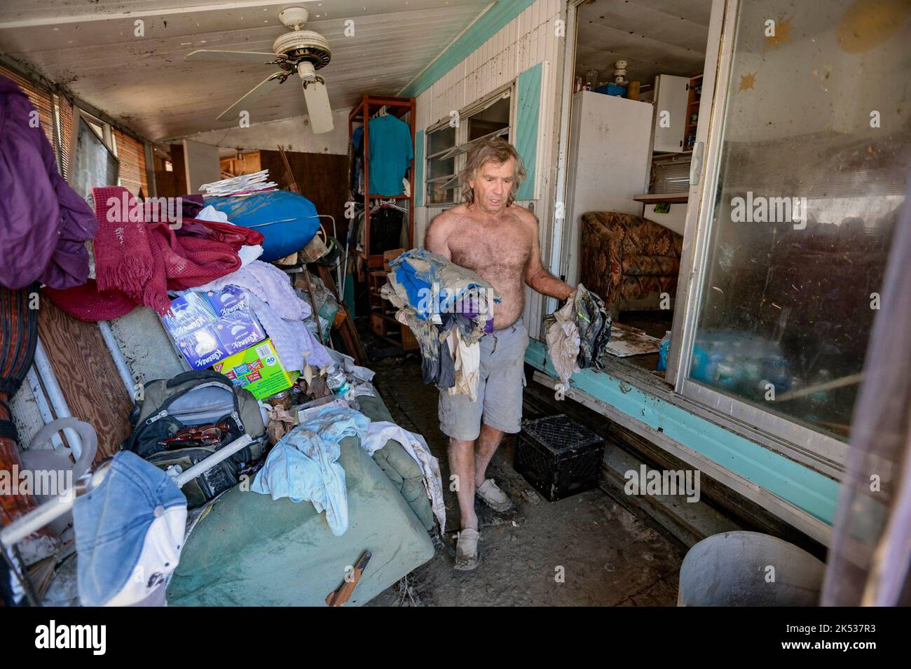 Kim Burke attempts to salvage clothing from his home filled with mud ...