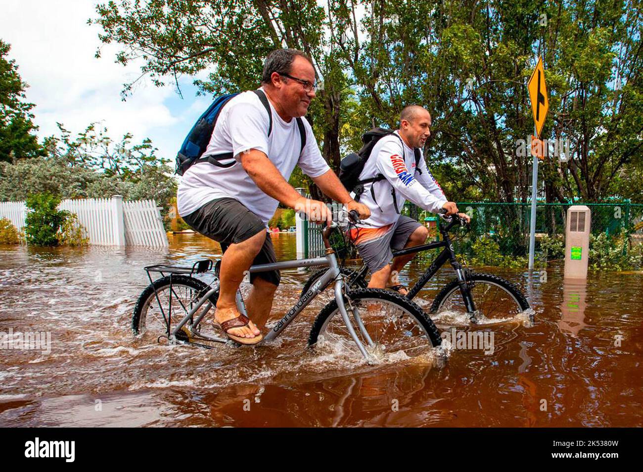 Bicyclists peddle through the flood waters due to the effects of ...