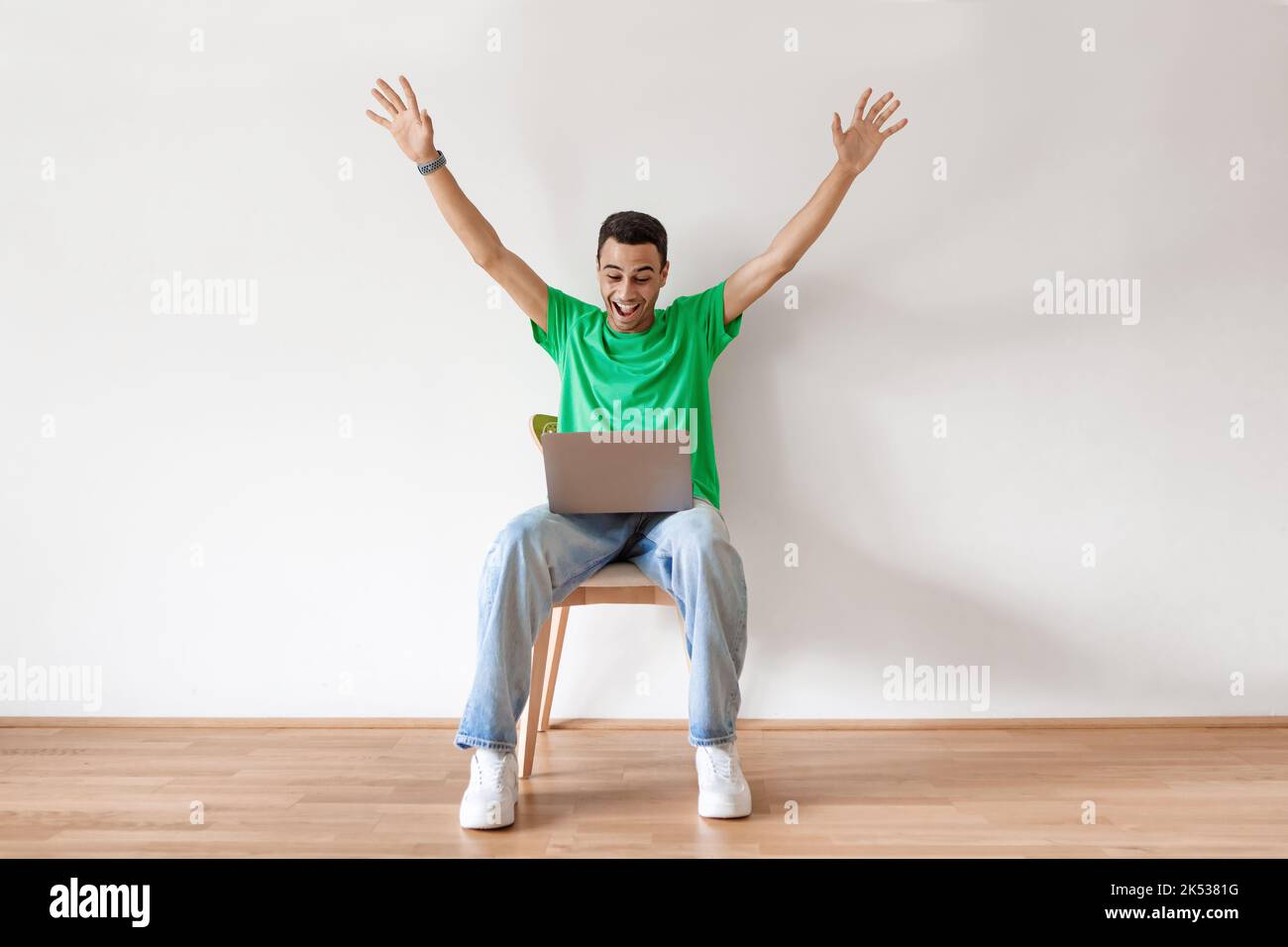 Overjoyed arab man in casual sitting on chair over white wall with ...