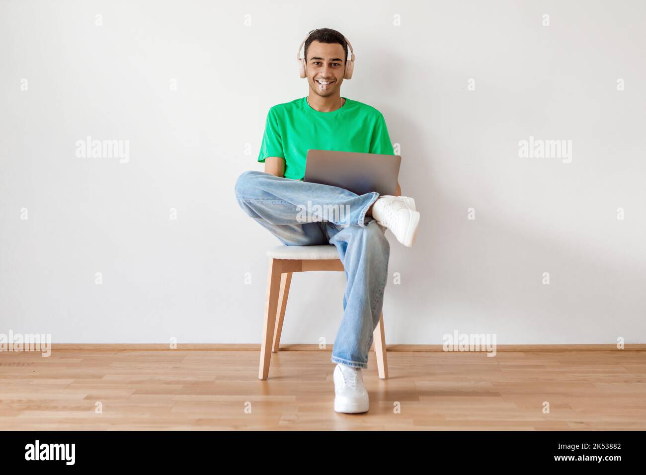 Happy middle eastern man using laptop and wearing wireless headphones ...