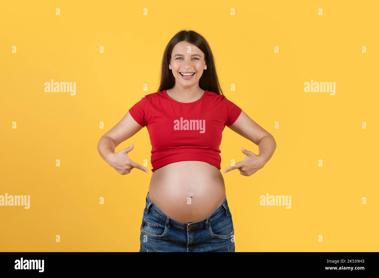 Cheerful Young Woman Pointing At Her Big Pregnant Belly With Two ...