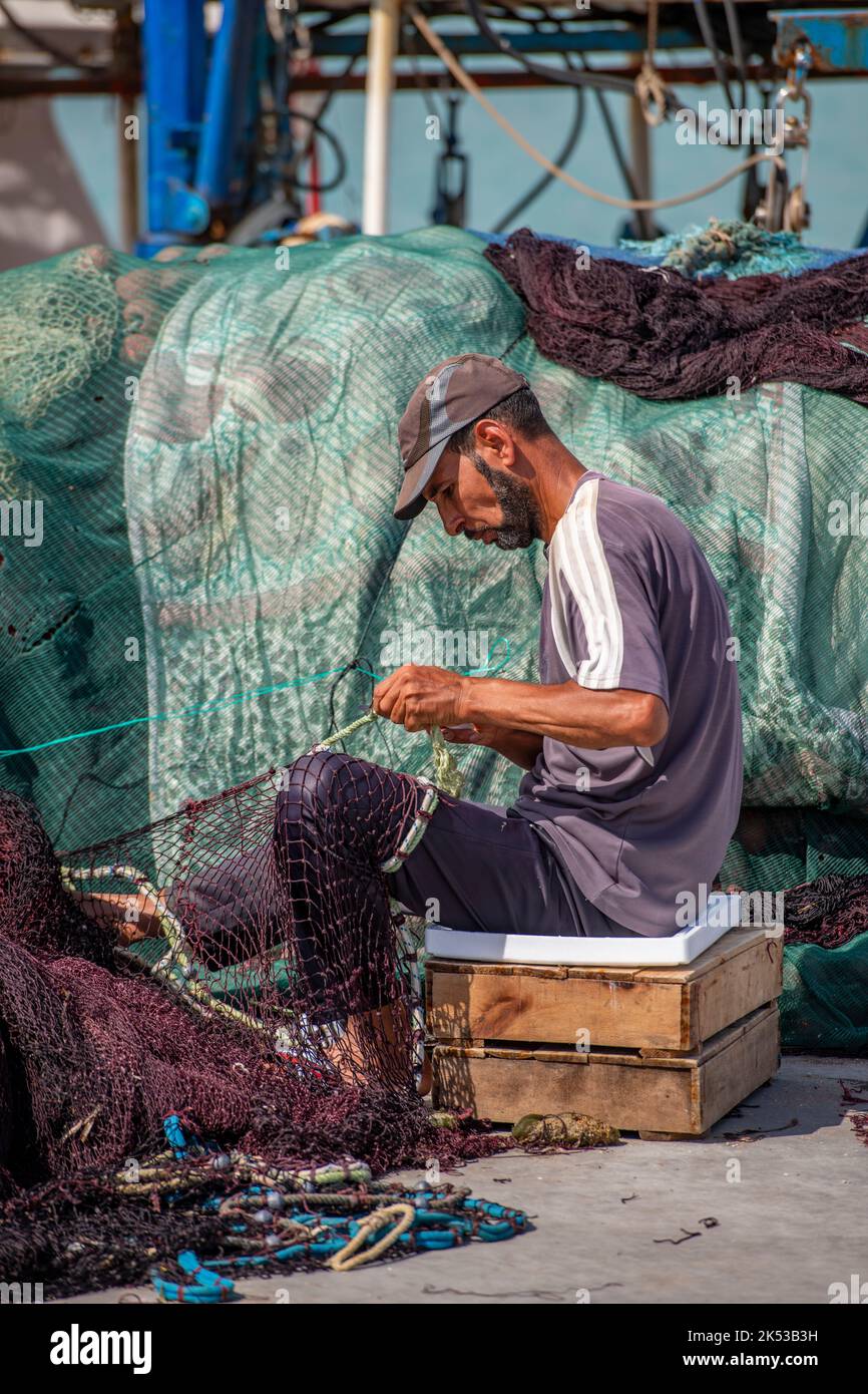 greek fisherman mending trawler nets on the dockside or harbour side in ...