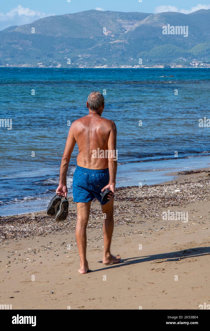 older man walking along a beach wearing blue shorts, middle-aged man ...