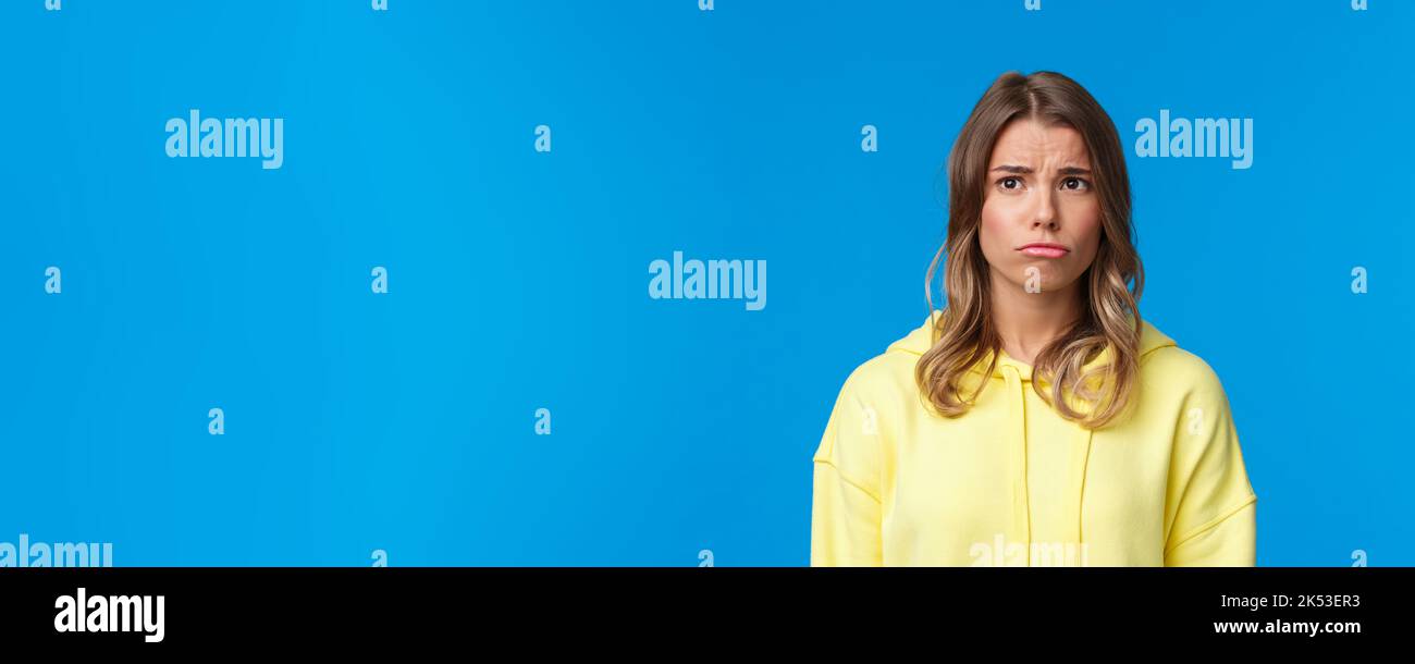 Close-up portrait gloomy sad cute jealous blond girl in yellow hoodie, pouting looking with ...