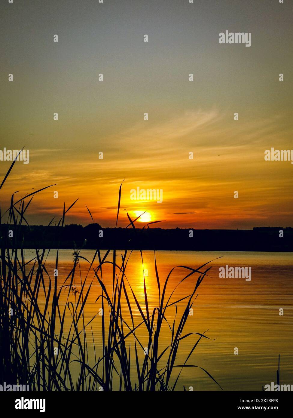 A vertical shot of the bright sun in sunset sky shining over the lake ...