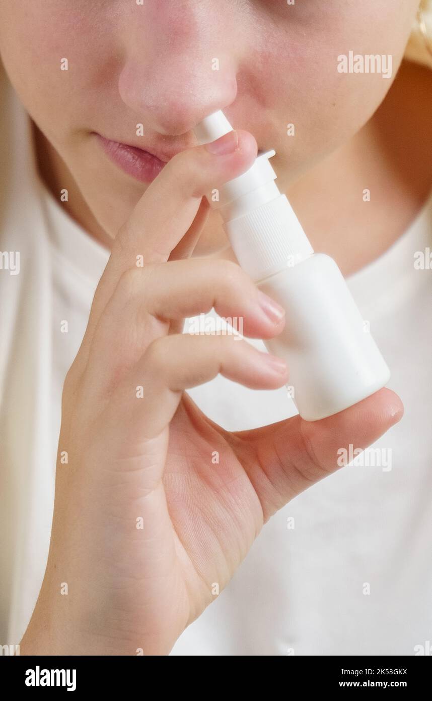 A girl with a cold treats a runny nose with a nasal spray. Vertical ...
