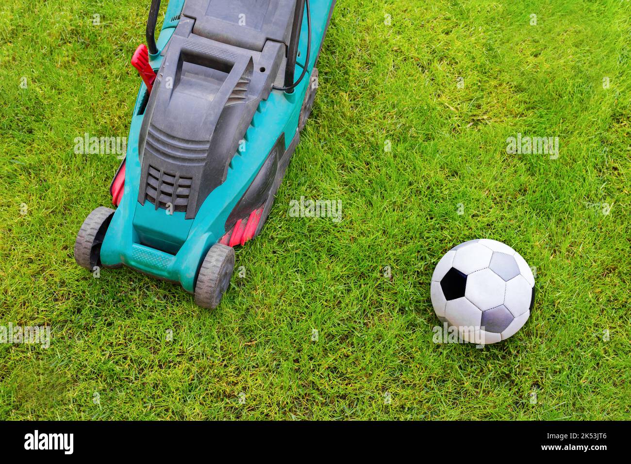 A football ball and a lawn mower in the green grass. A view from above ...