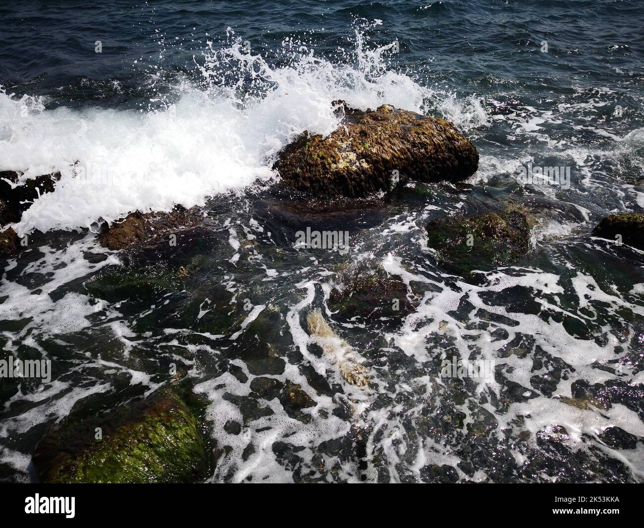 A wave hitting the surface of rocks on a shore, forming a splash Stock ...