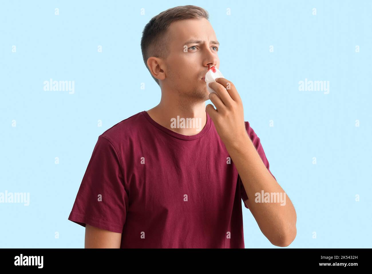 Young man wiping nosebleed with tissue on blue background Stock Photo ...