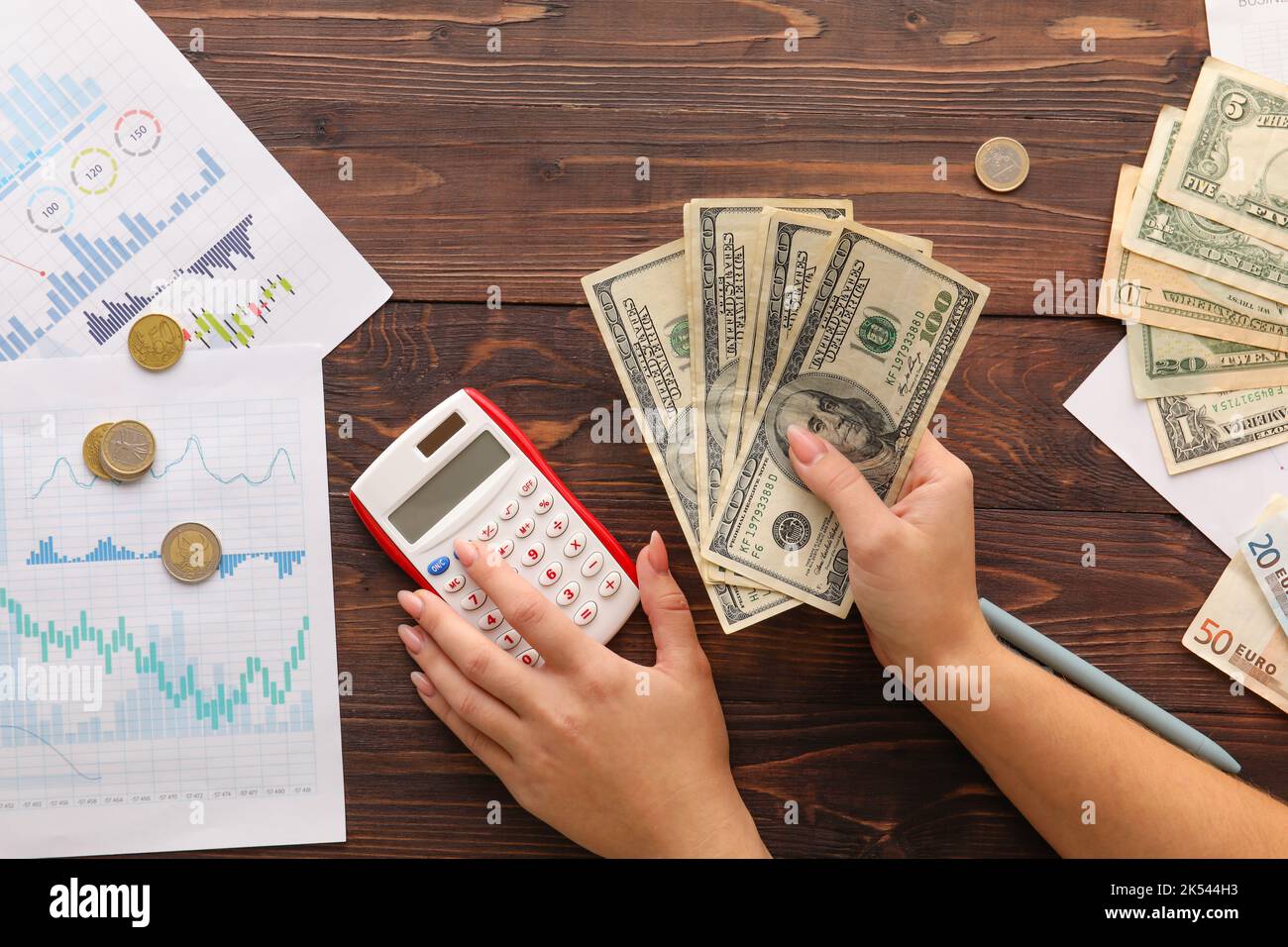Woman with dollar banknotes, calculator and diagrams on dark wooden ...
