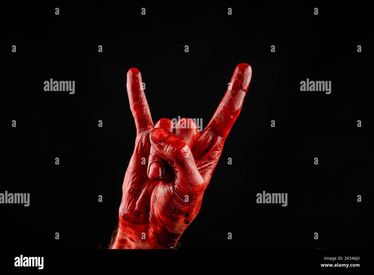 A man's hand covered in blood shows a goat sign on a black background ...