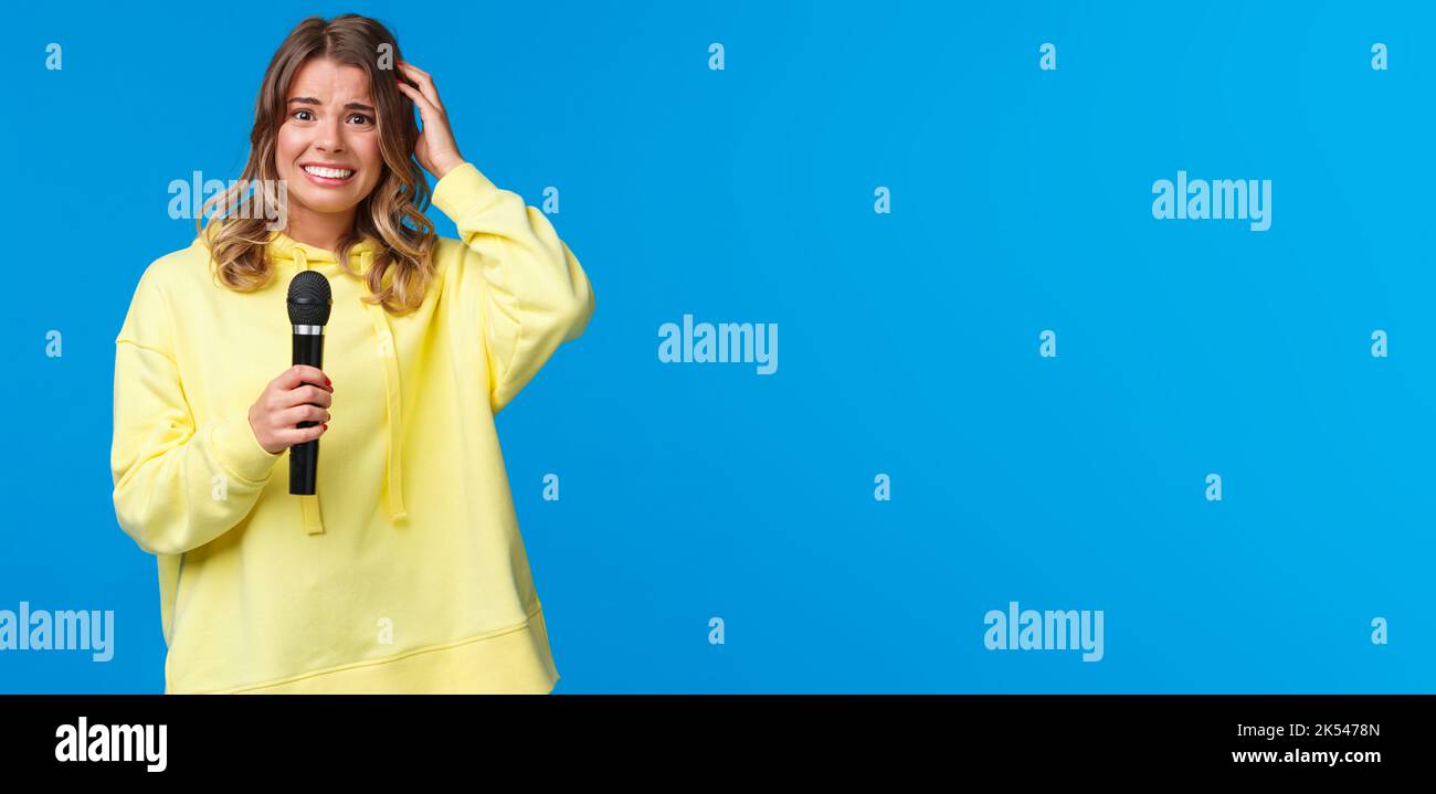 Embarrassed girl holding microphone awkward smiling and scratch head as ...