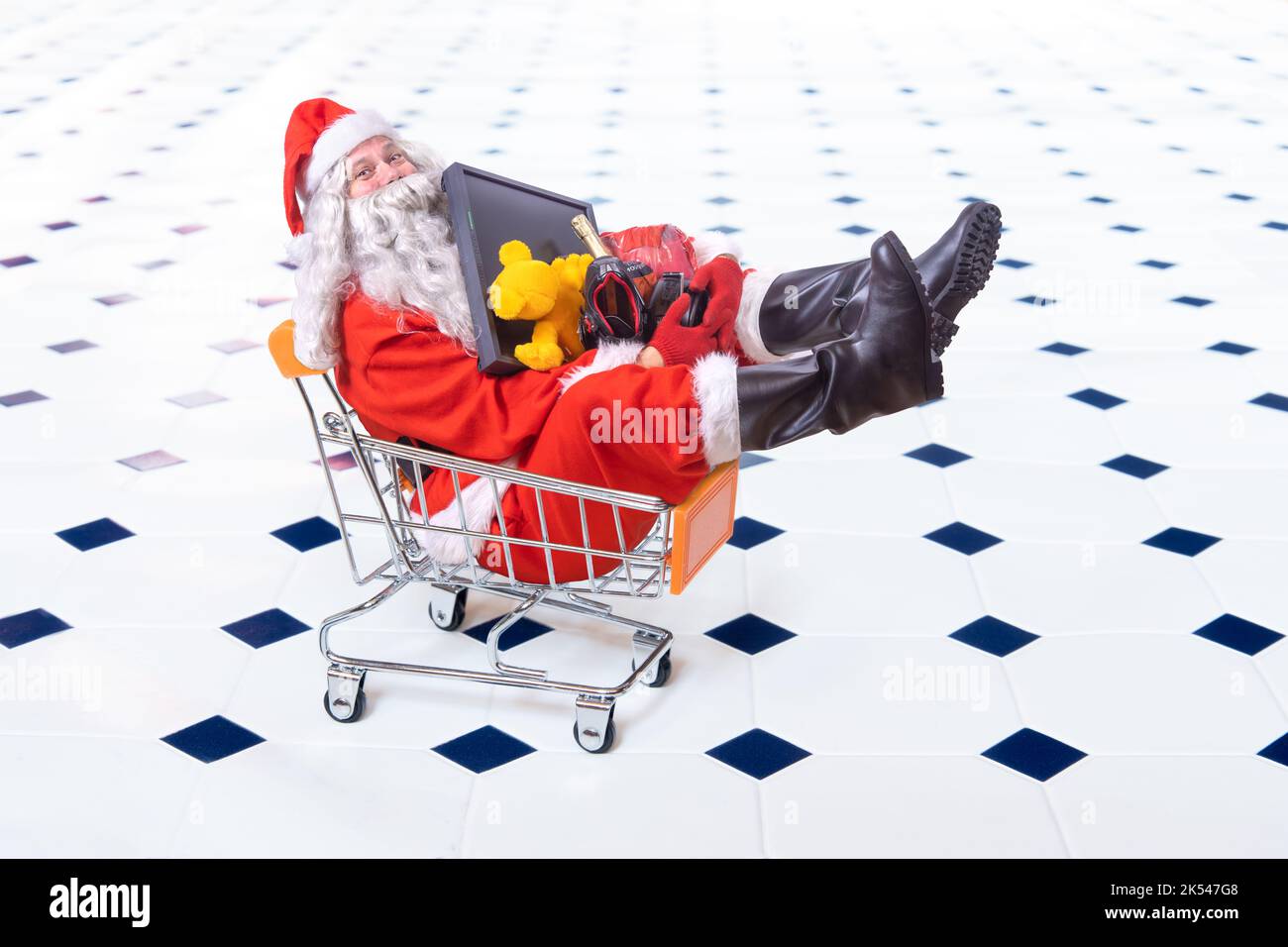 Cheerful Santa Claus is sitting in a shopping cart with his arms full ...