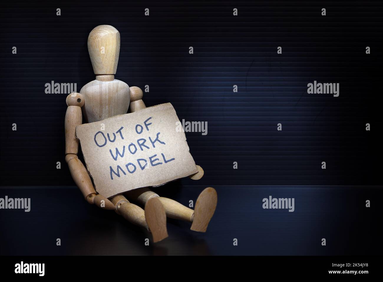 A wooden Artists Mannequin sitting down holding an Out Of Work Model ...