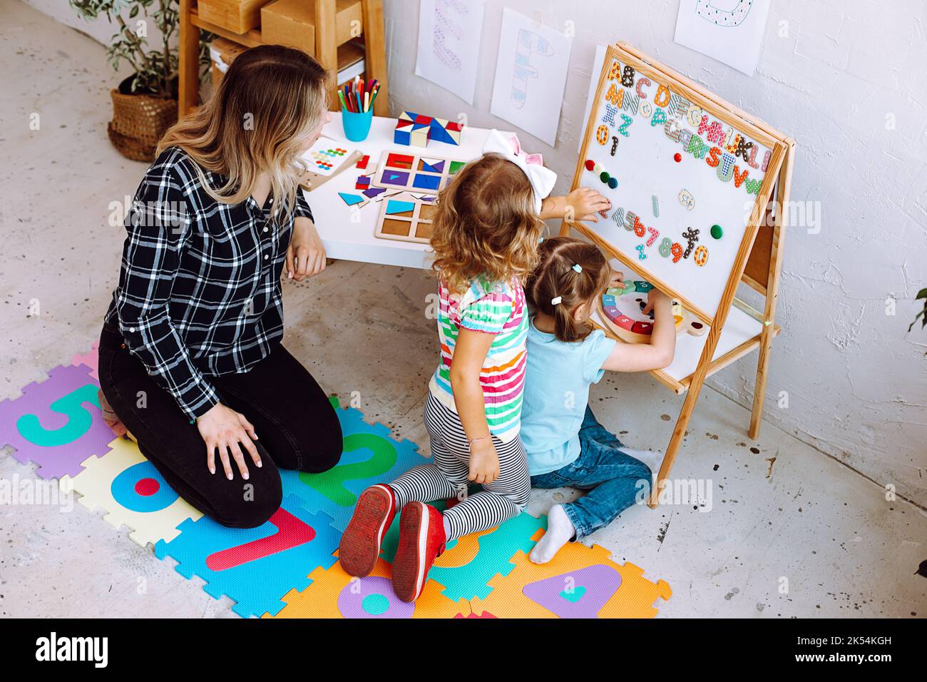 Educator teach little children read and count while sitting on floor in playing room. Little ...