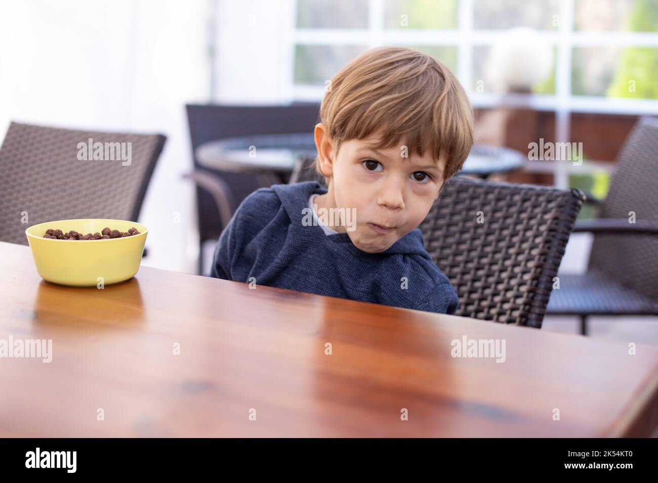 Little boy sit on chair at table in empty hall in cafe and staring chew ...