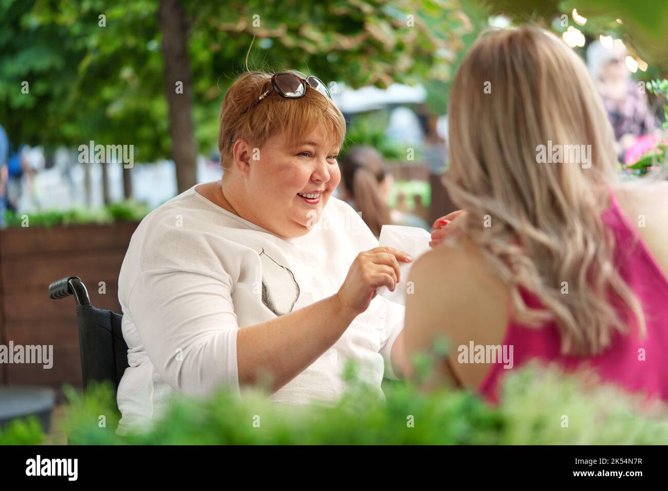 Woman wheelchair user dining at a restaurant with her young daughter ...