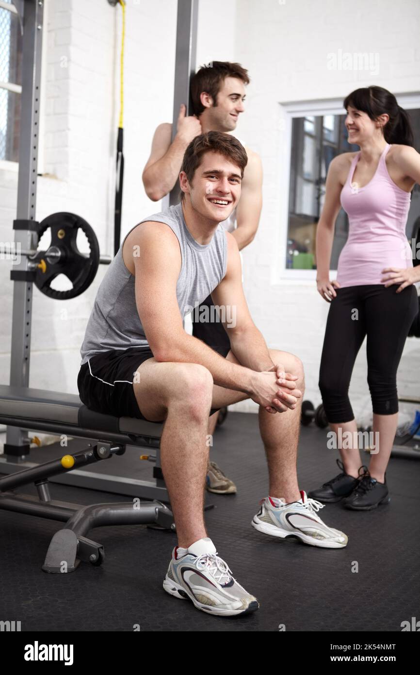Gym buddies. Young man smiling at the camera with two other gym members ...