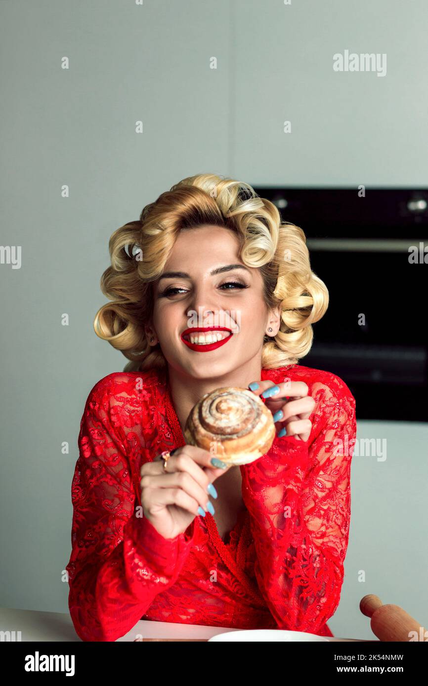 Beautiful housewife in a red robe with a bun in her hands Stock Photo ...
