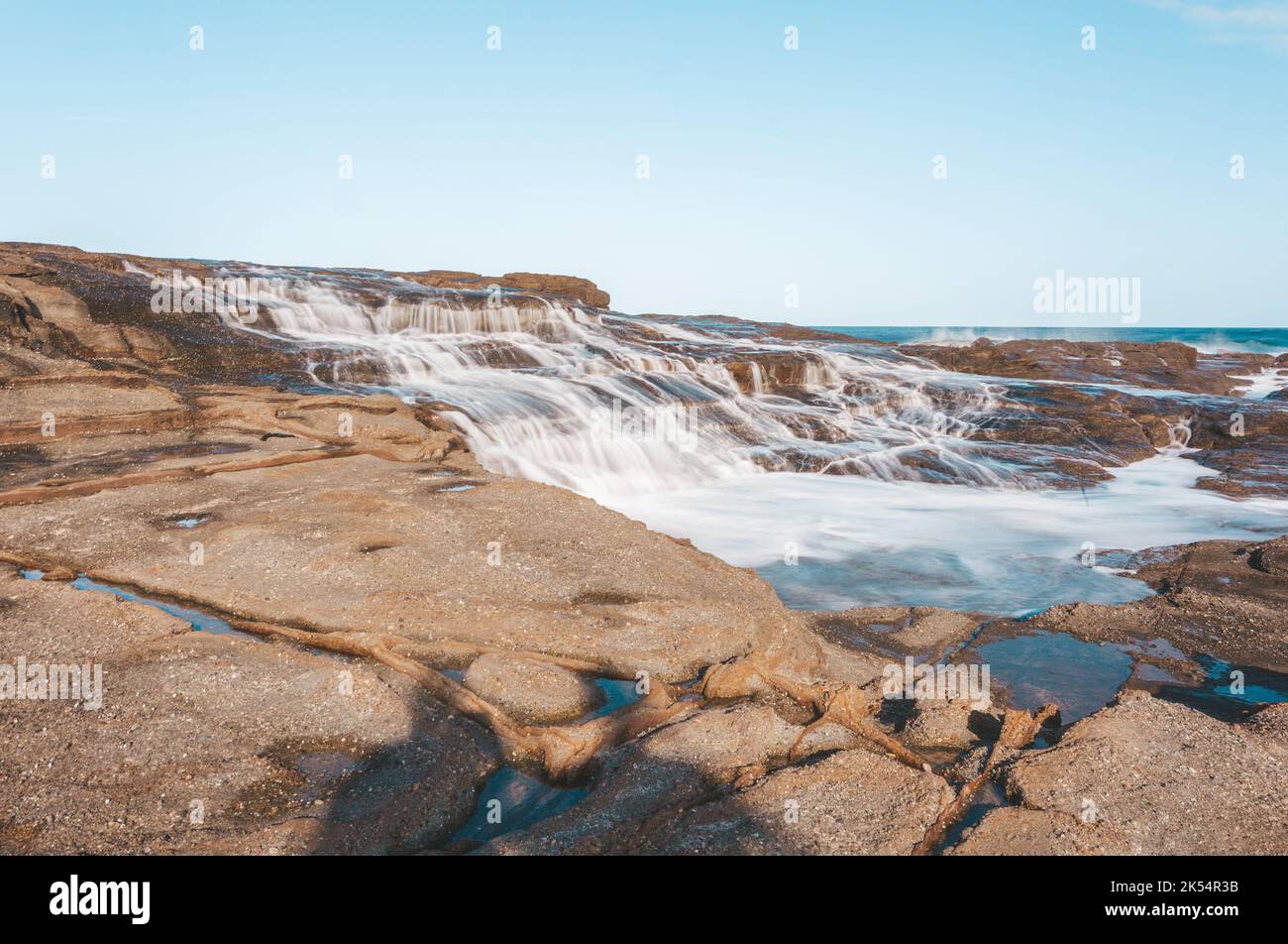 Milky ocean cascades flowing over honey coloured rocks. Australia Stock ...