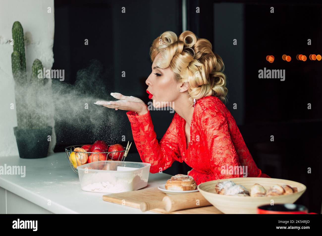 A beautiful woman in a red robe holds flour on her hand and blows air ...