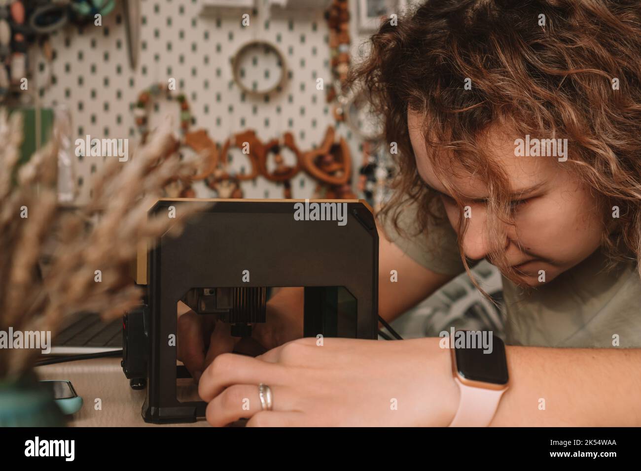 Curly haired woman holds item in desktop laser wood burning machine to ...
