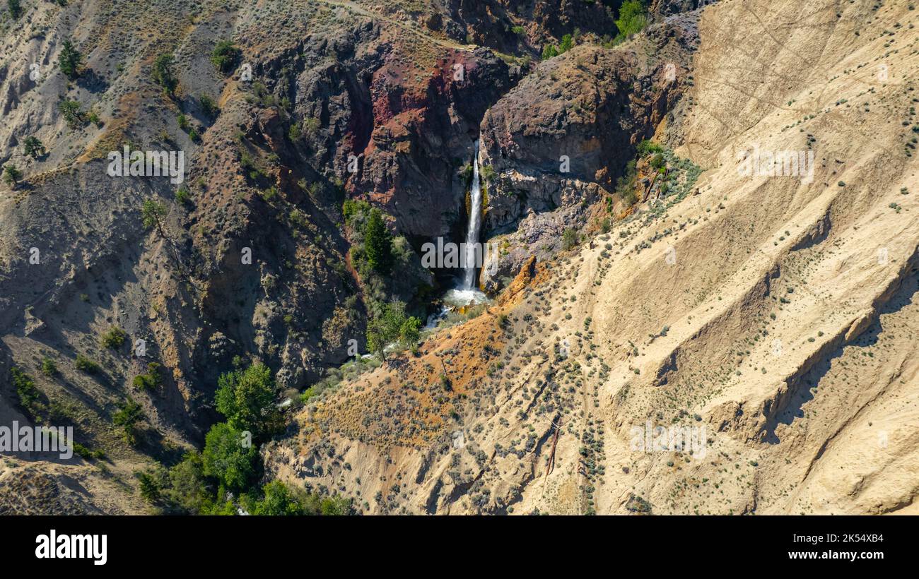An aerial of a waterfall cutting through a mountain and spilling into a ...