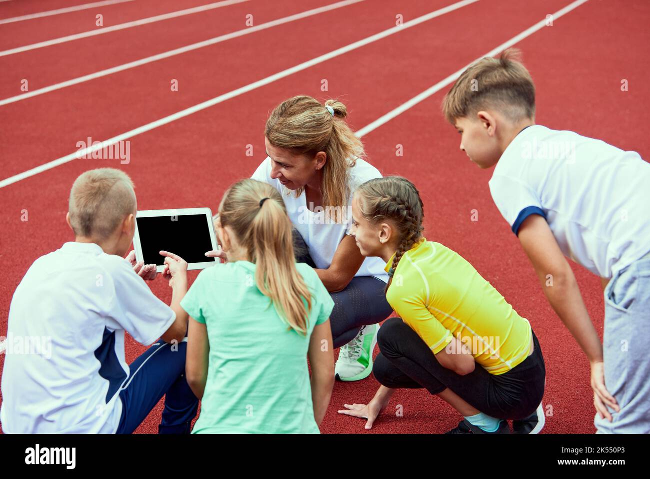 Female coach training athletes. Group of children before running on ... Female coach training athletes. Group of children before running on ...