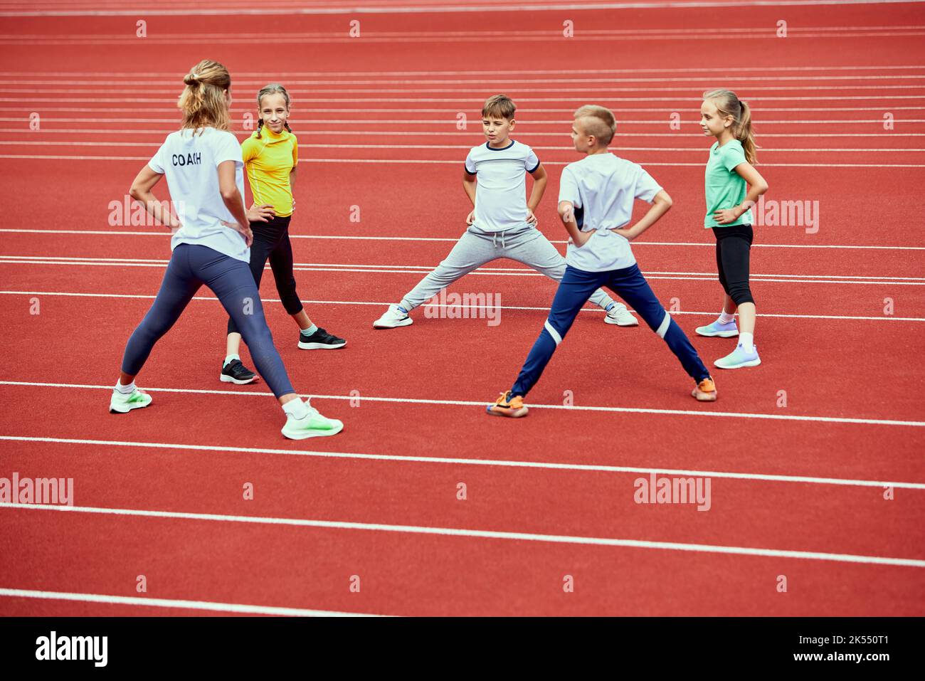 Female coach training athletes. Group of children running on treadmill ...