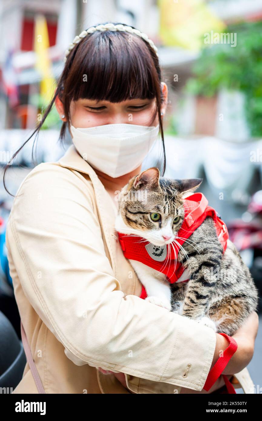 A young Thai lady holds her beautiful cat wearing a little red jacket ...