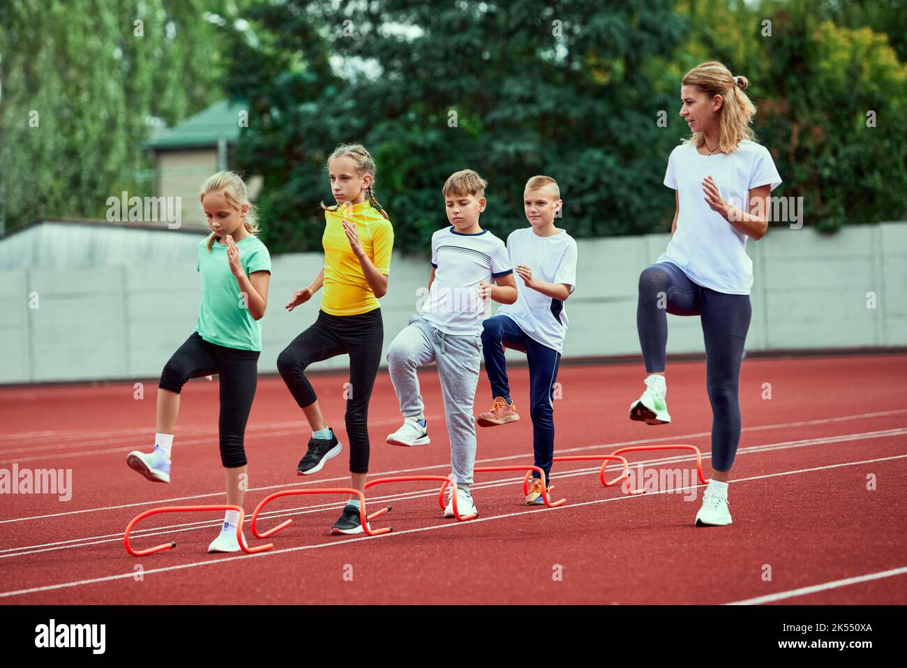 Female coach training athletes. Group of children running on treadmill ...