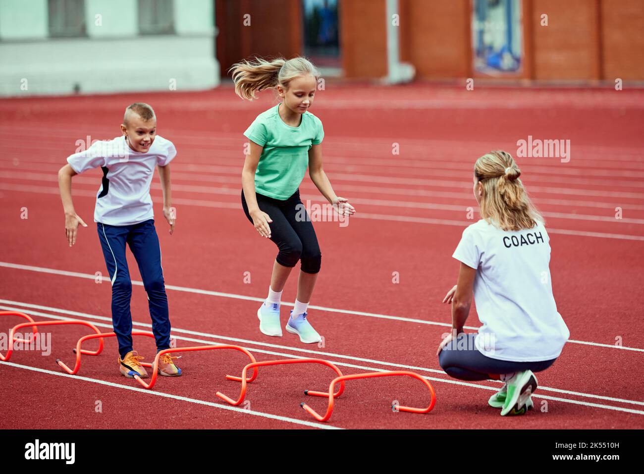 Female coach training athletes. Group of children running on treadmill ...