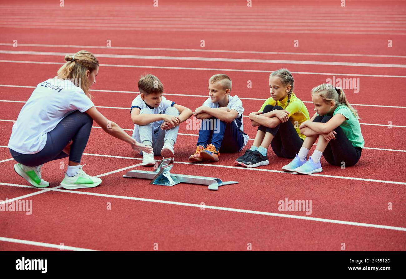 Female coach training athletes. Group of children running on treadmill ...