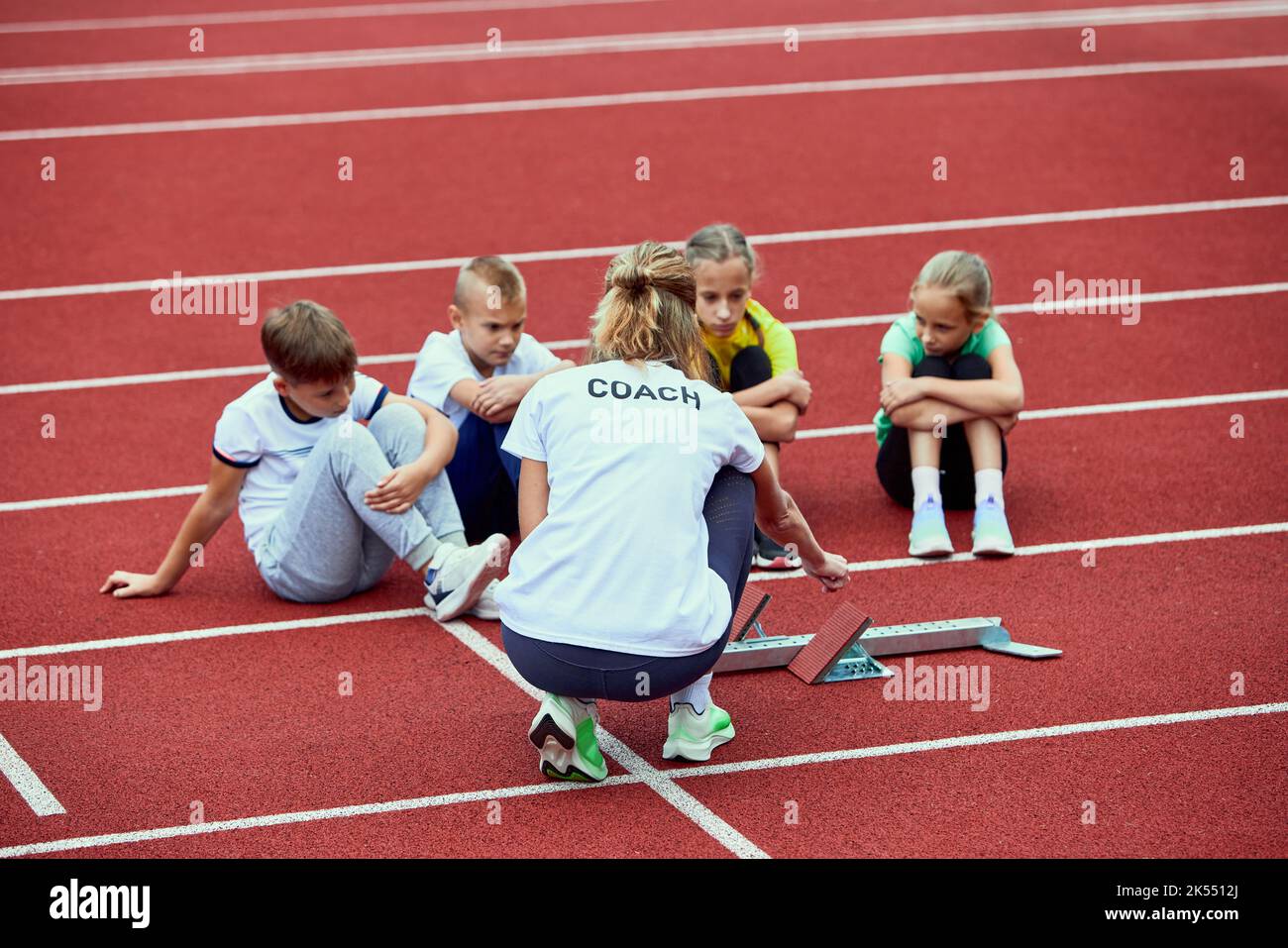 Female coach training athletes. Group of children running on treadmill ...