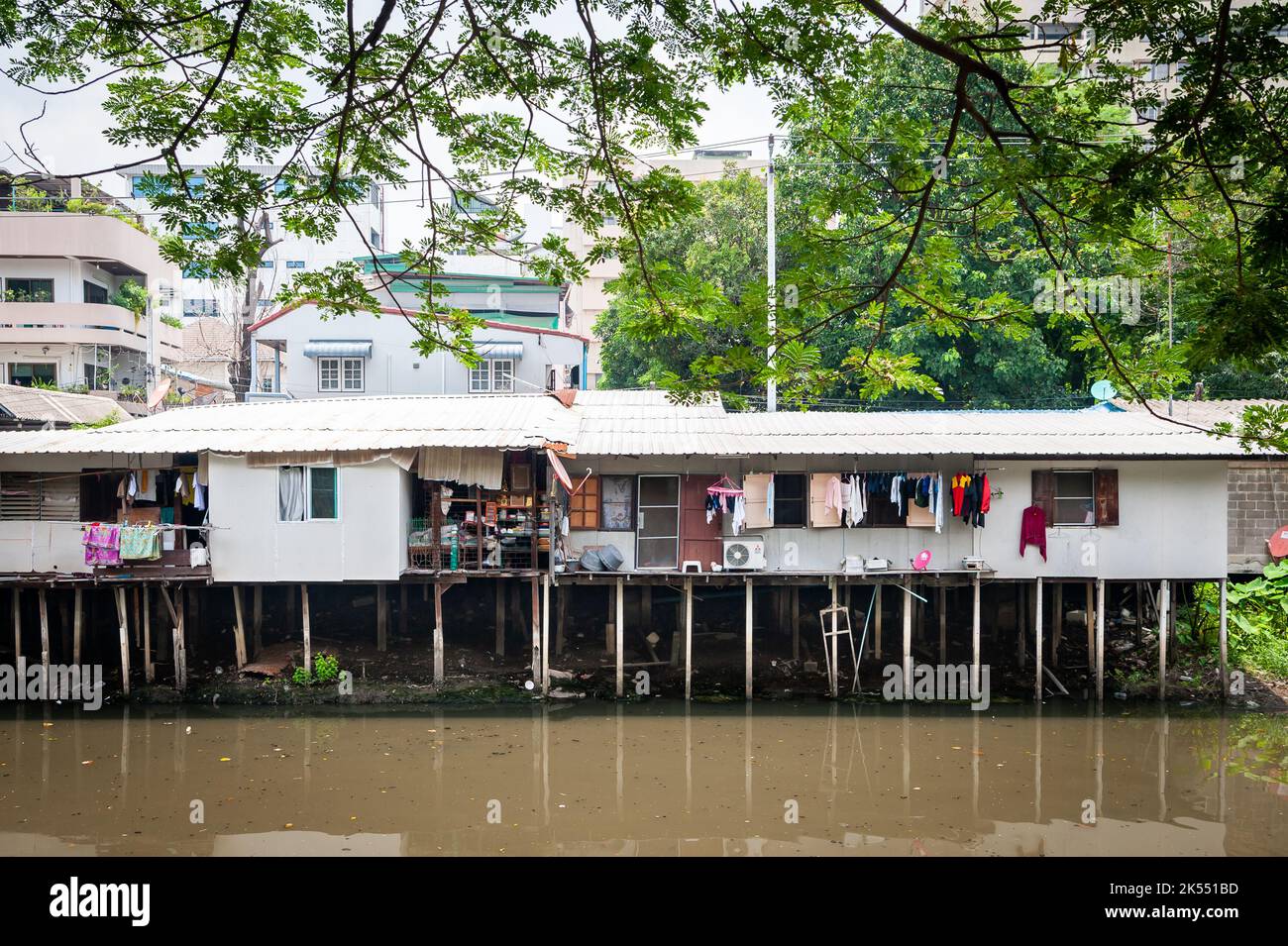 Traditional old Thai houses on stilts above a river contrast against ...