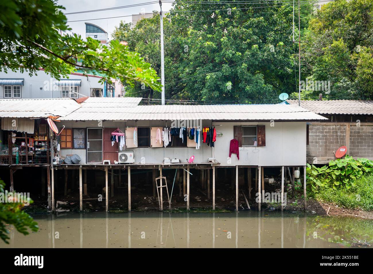 Traditional old Thai houses on stilts above a river contrast against ...
