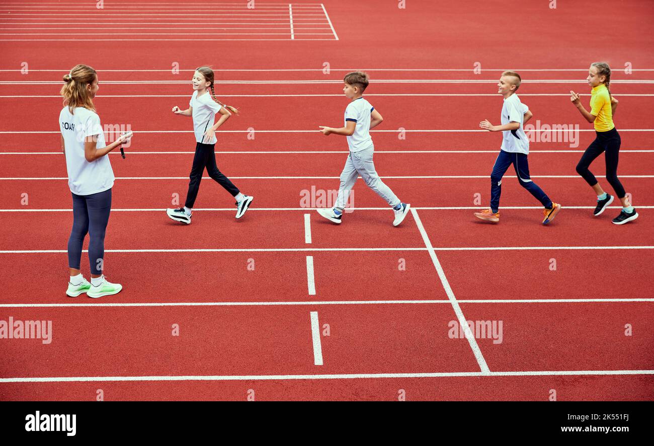 Female coach training athletes. Group of children running on treadmill ...