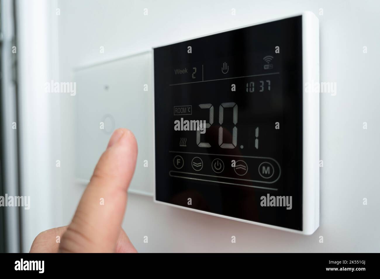 Close-up of a male hand adjusting a modern wall-mounted digital ...