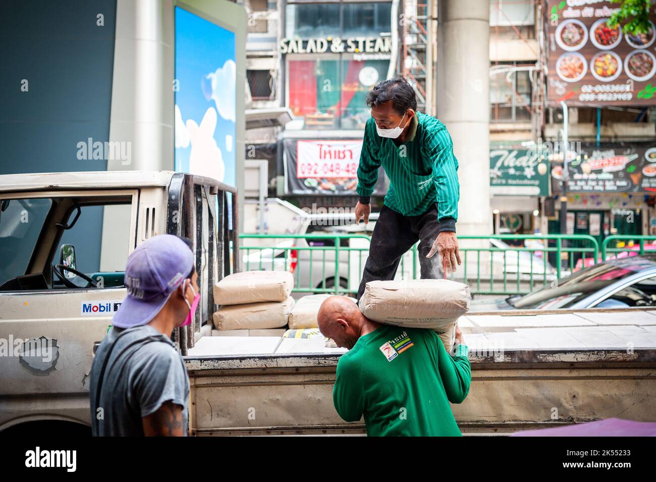 Thai construction workers unload cement or gravel from the back of a ...