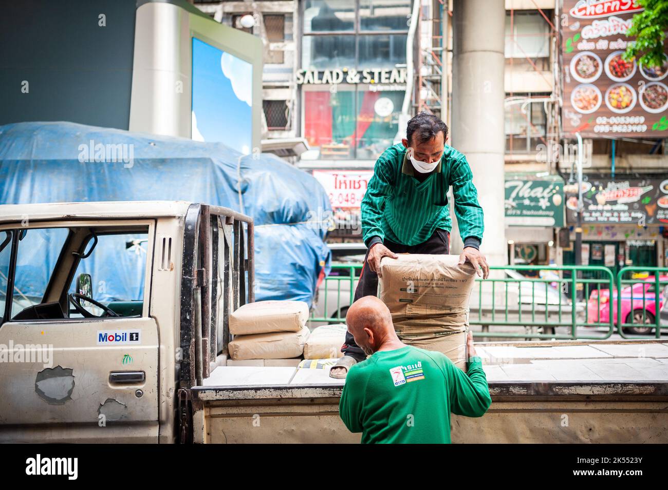 Thai construction workers unload cement or gravel from the back of a ...